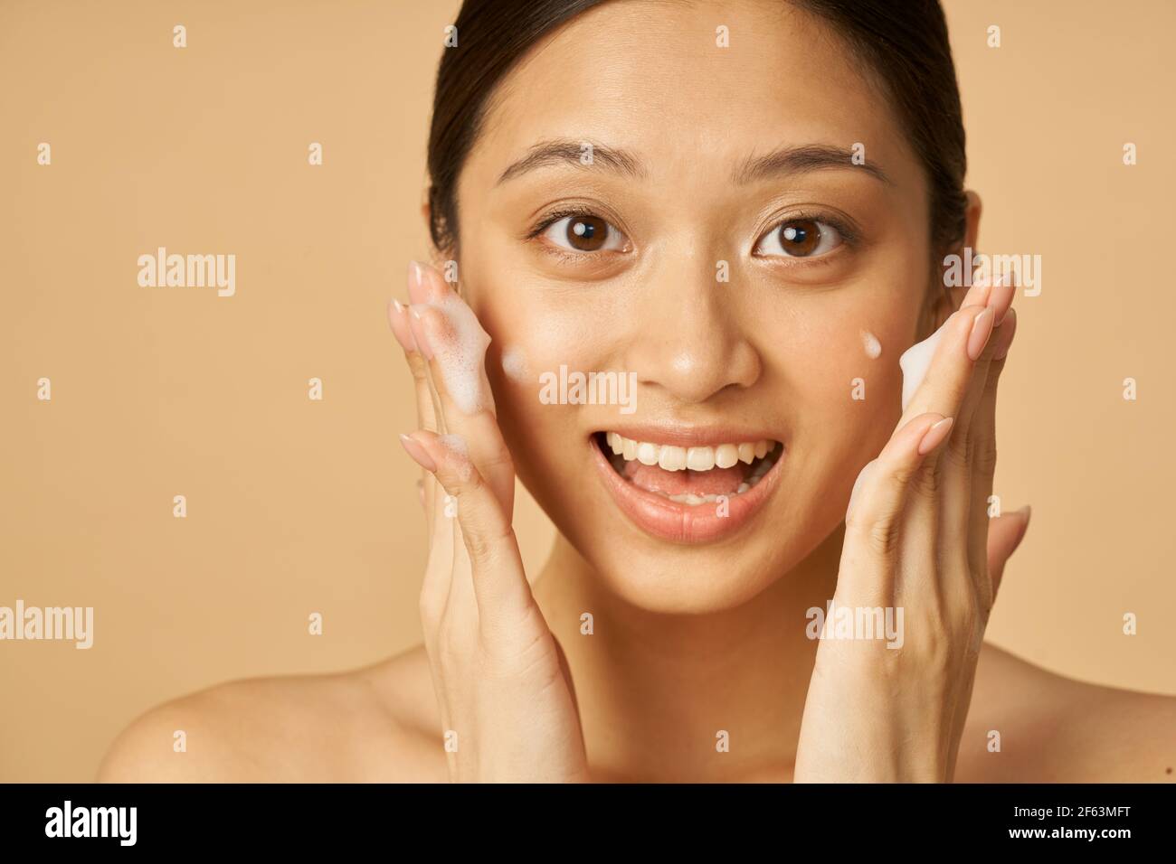 Studio portrait of excited young woman smiling at camera while applying ...