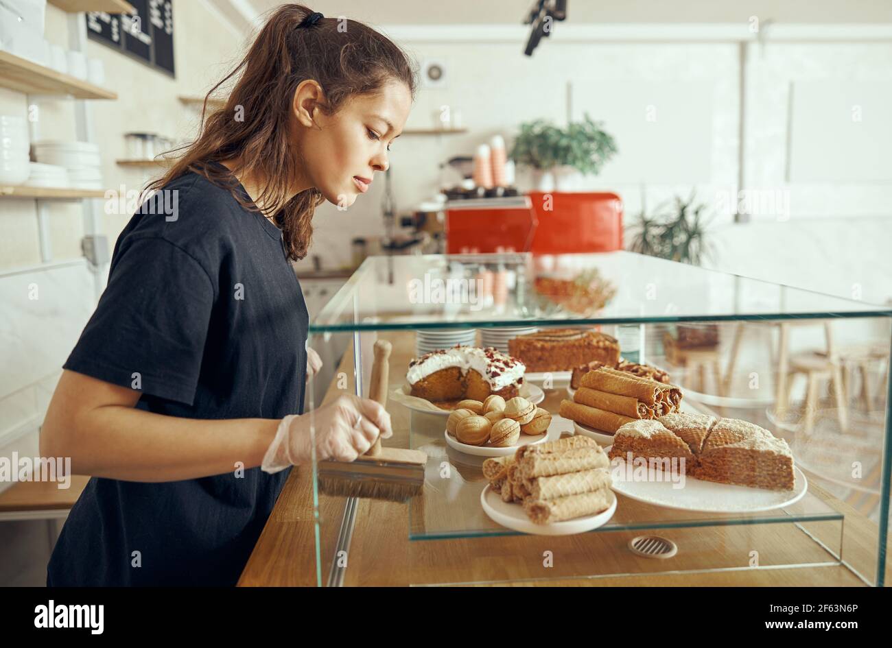 Female barista at showcase with desserts in cafe. Young worker of sweet ...