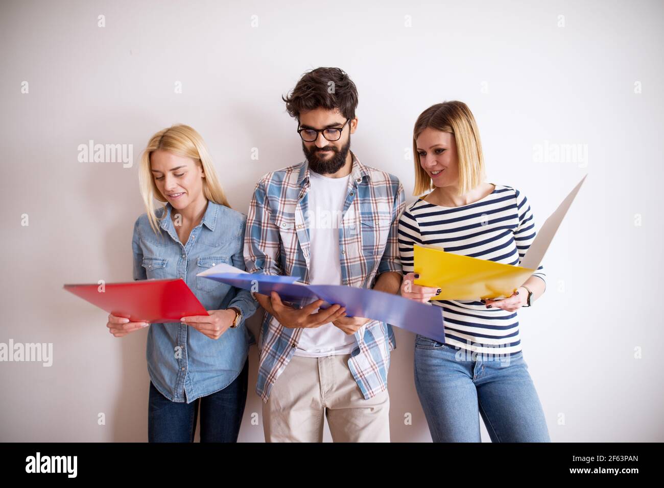 Group of young smart people leaning against the wall and looking at ...