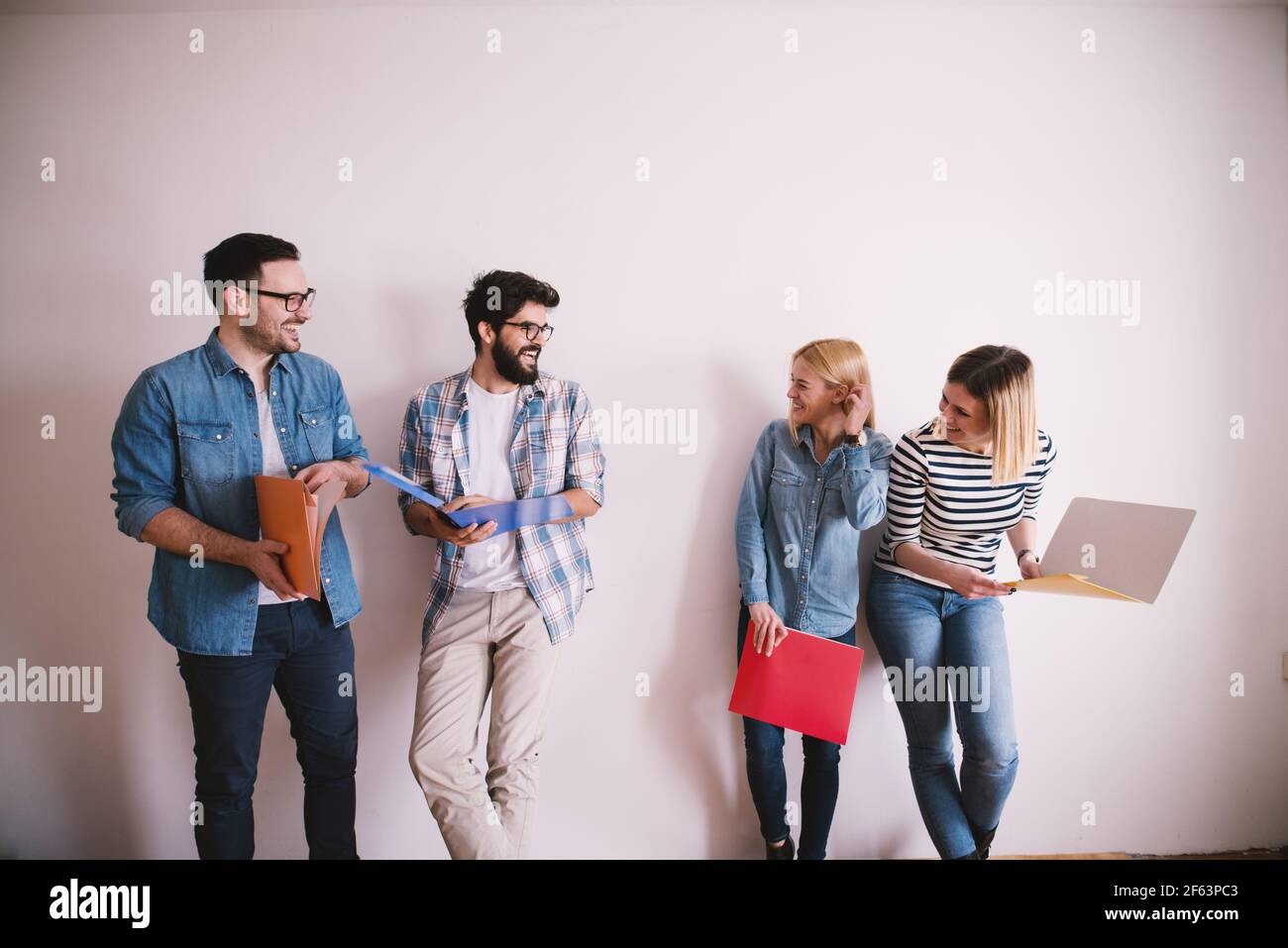 Two groups of young men and women leaning against the wall having a ...