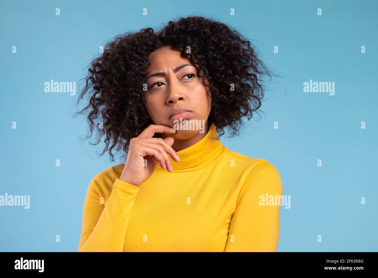 Thinking mixed race woman looking up on blue studio background. Pensive ...