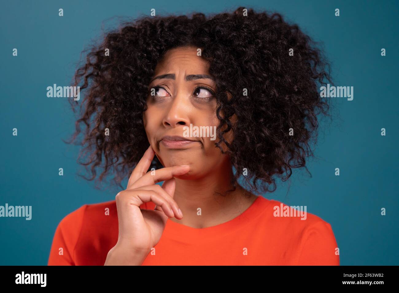 Thinking mixed race woman looking up on blue studio background. Pensive ...