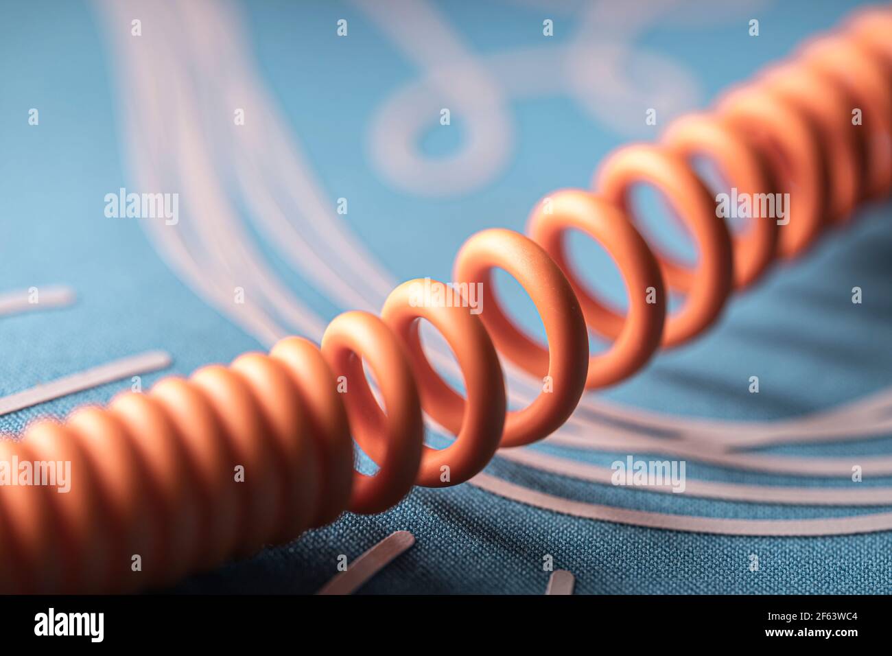 Twisted orange telephone cord on a blue background. Closeup photo with a low depth of field ...