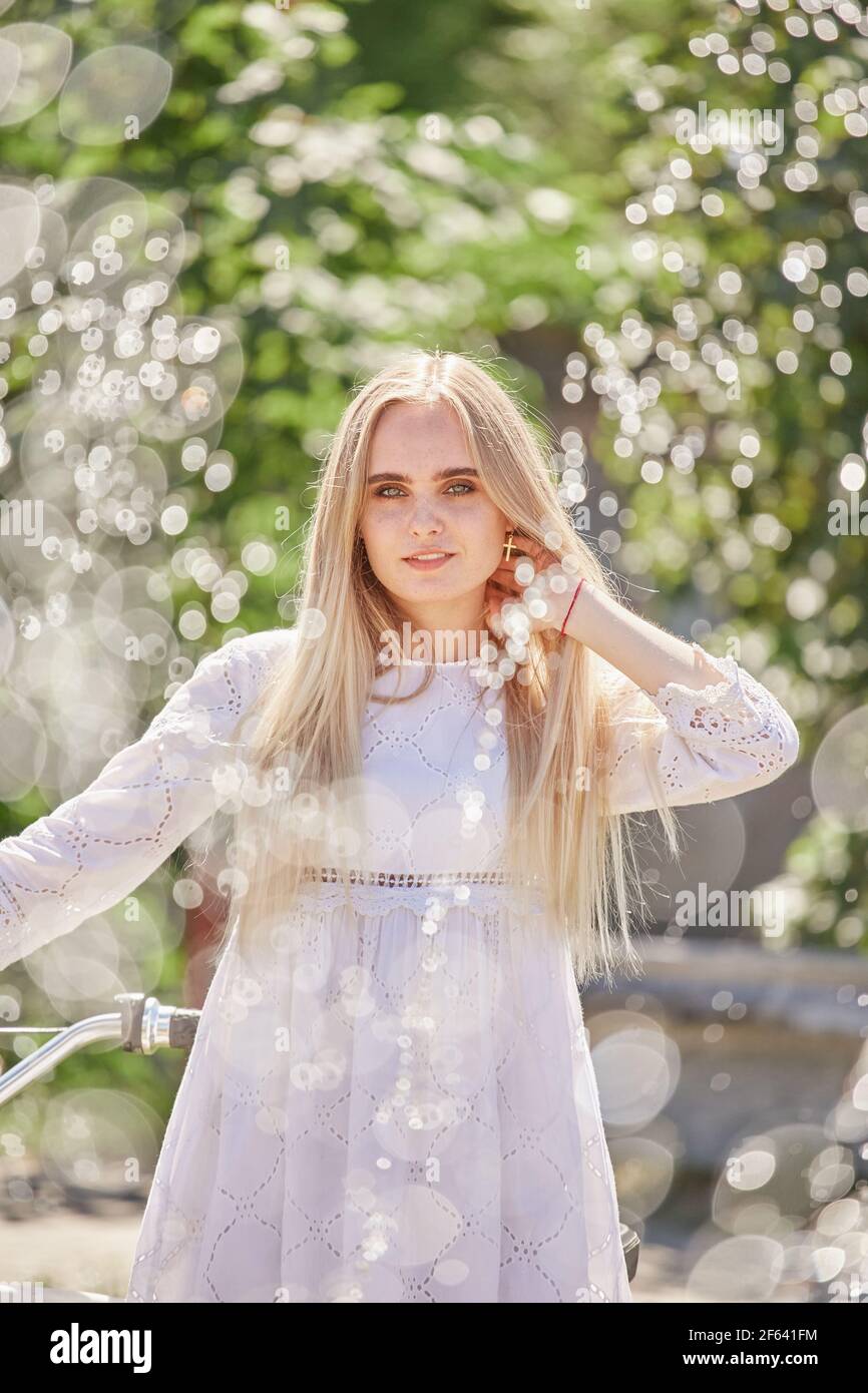 pretty blond woman in white dress with bike near fountain in sunny ...