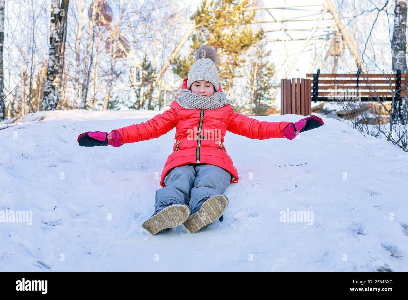 Young cheerful caucasian girl in a bright sport suit is sledding down ...