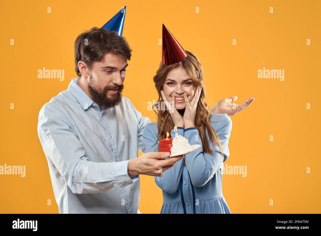 Birthday party man and woman on a yellow background in hats with a cake ...