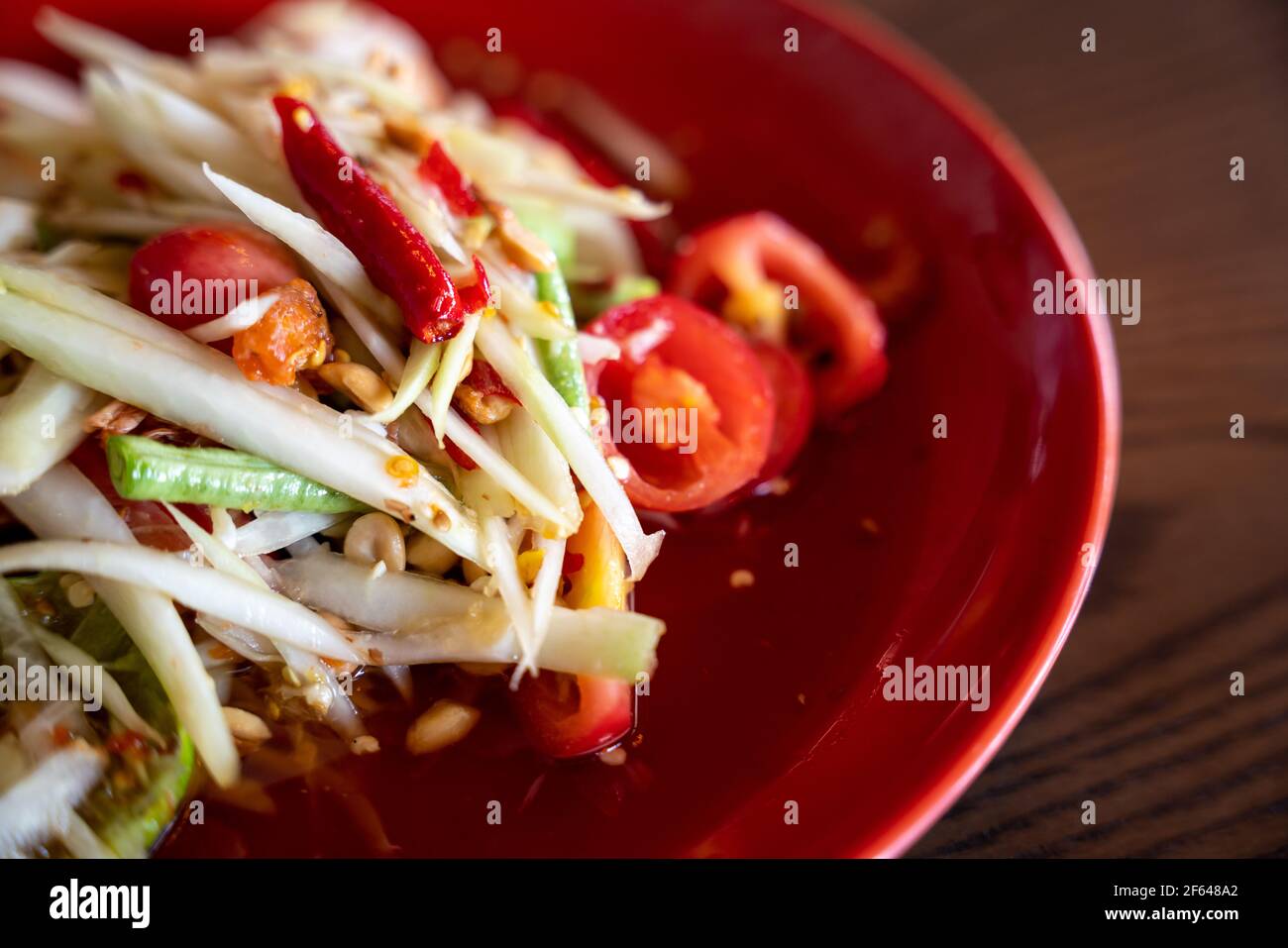 som tam thai, green papaya salad and spicy in red plate on wooden ...