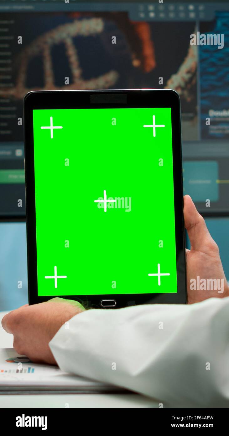 Close up of biochemist sitting at workplace in laboratory using green mock-up screen tablet with ...