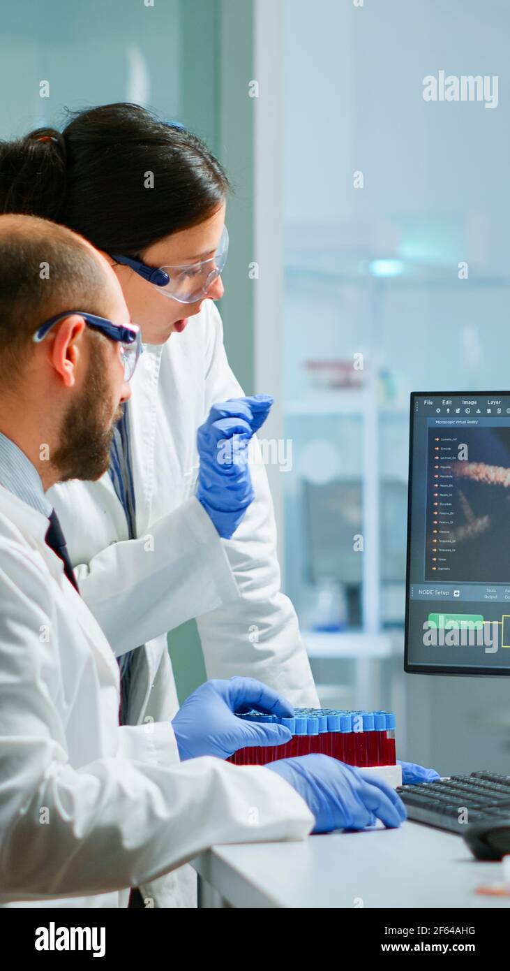 Team medical scientist conducting DNA experiments looking in computer ...