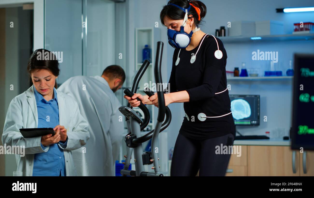 Woman athlete with mask running on cross trainer in sports science lab ...