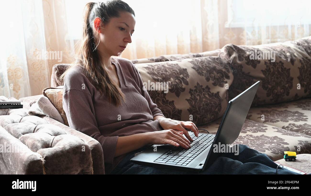 Young girl sitting on the couch at home, working remotely at the ...