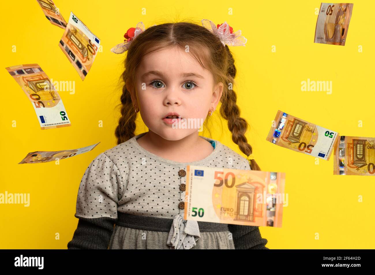 Little girl on a yellow background in the rain with money, euros flying ...