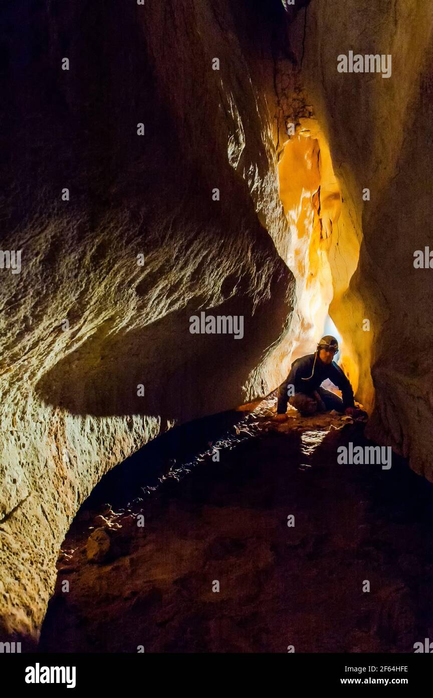 Speleologist exploring a deep cave discovering new underground passage ...