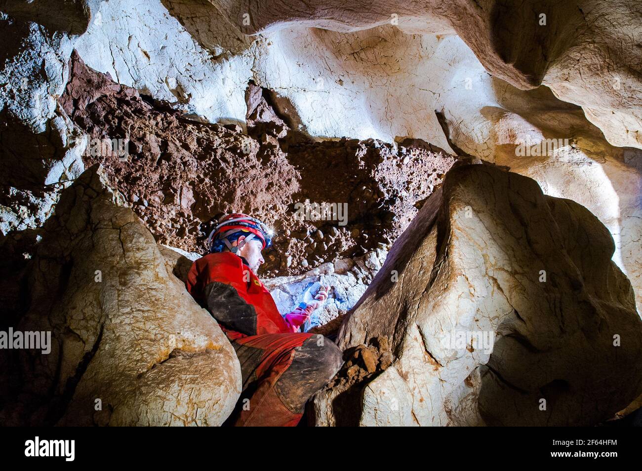 Geologist in red coverall and helmet studying limestone rocks deep in a ...