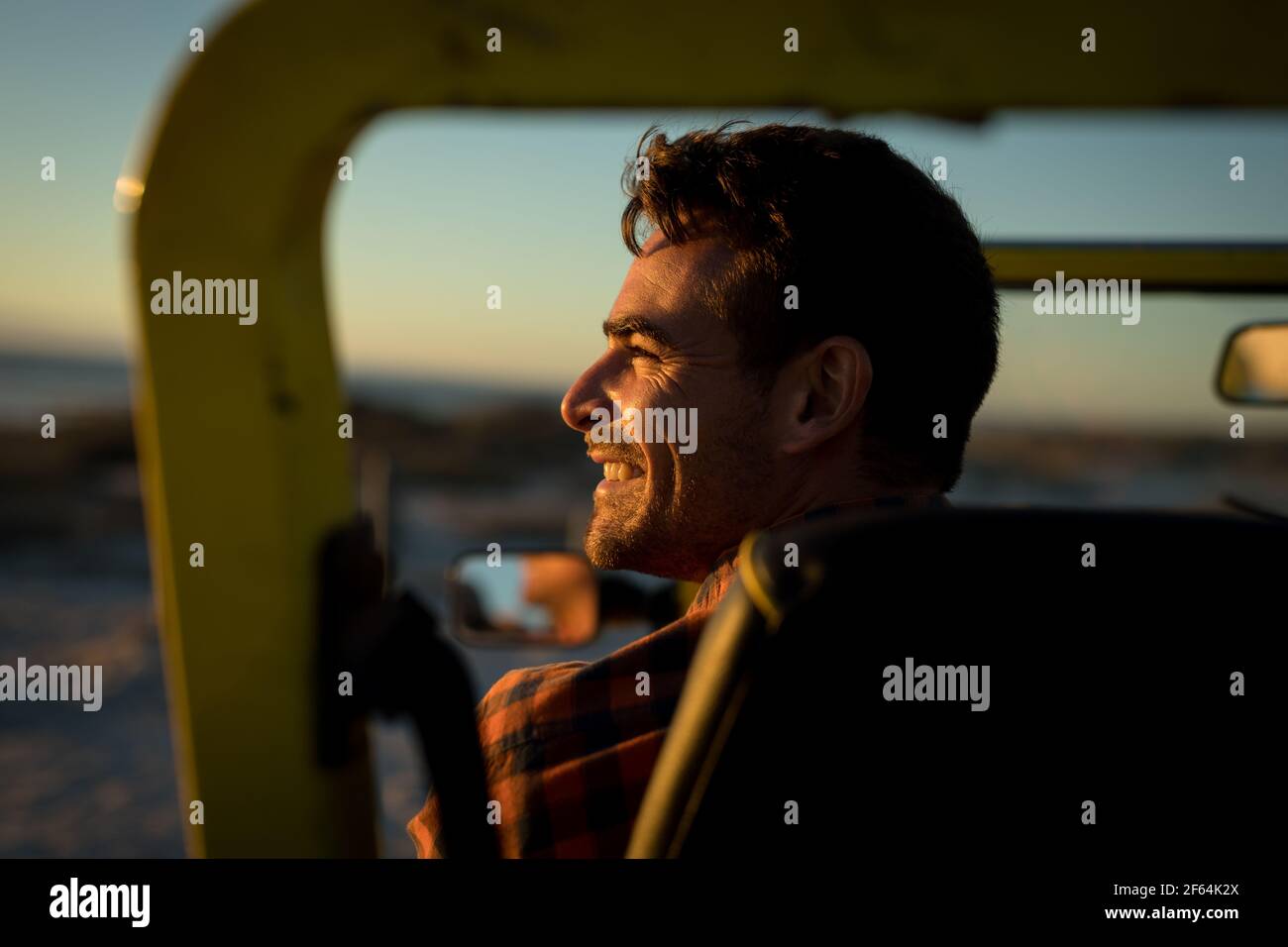 Happy caucasian man sitting in beach buggy by the sea during sunset ...