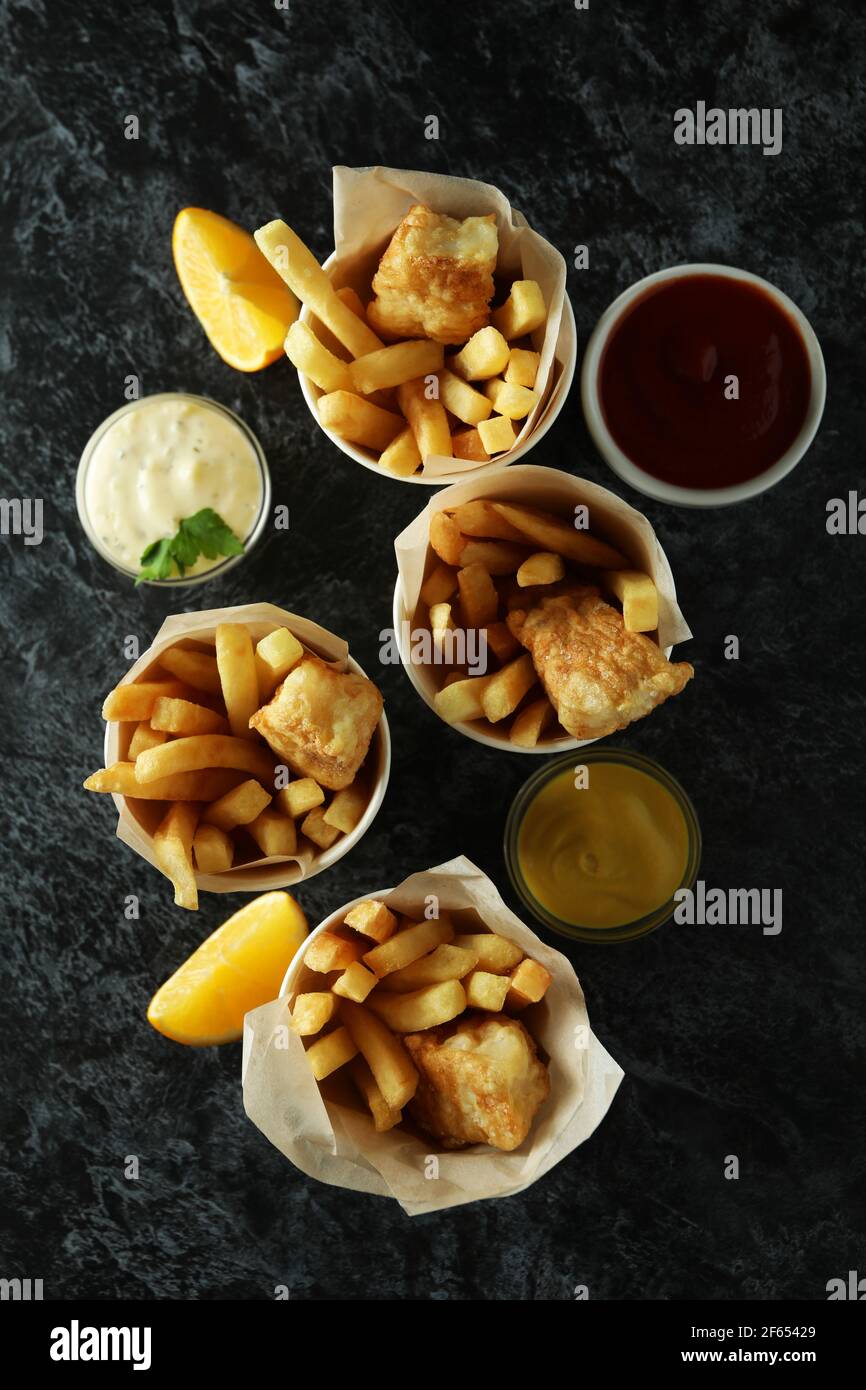 Paper cups with fried fish and chips, and sauces on black smokey ...