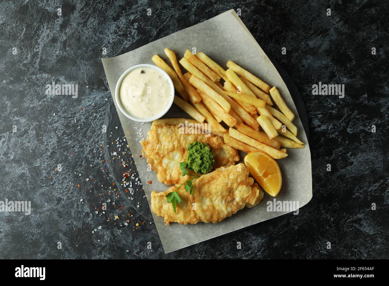 Baking paper with fried fish and chips on black smokey table Stock ...