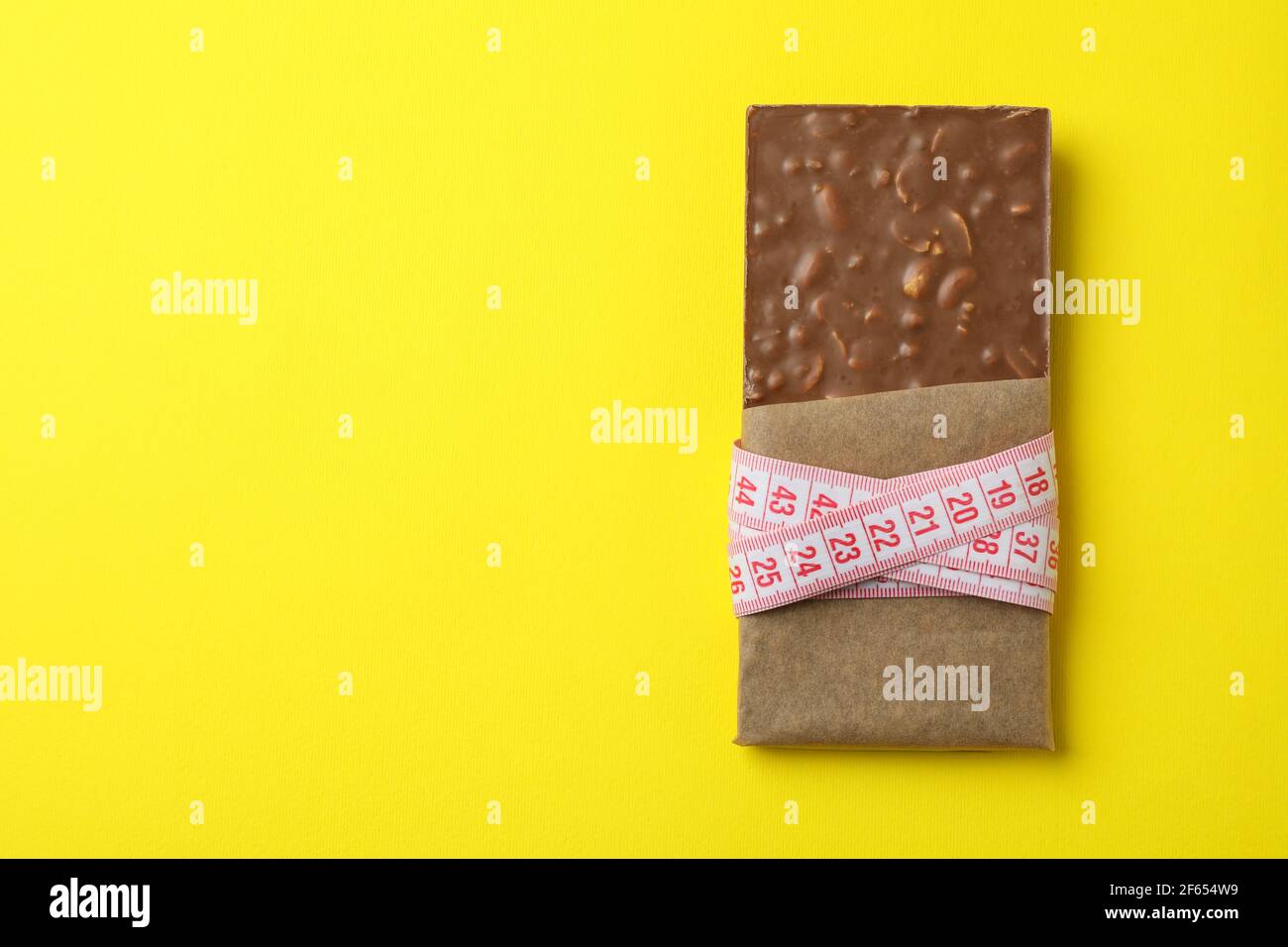 Chocolate bar with measuring tape on yellow background Stock Photo - Alamy