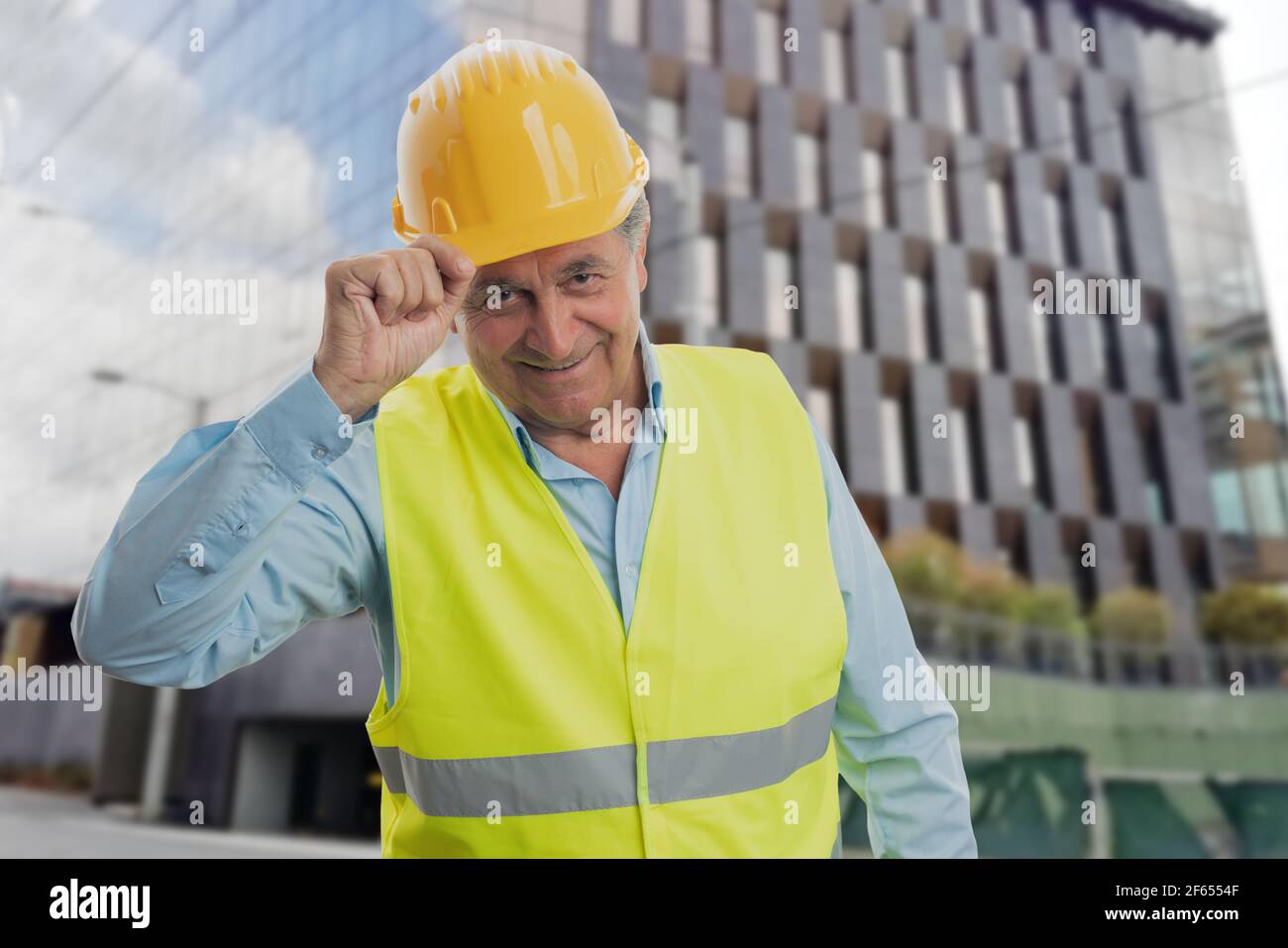 Old constructor man in work attire vest and yellow helmet making ...