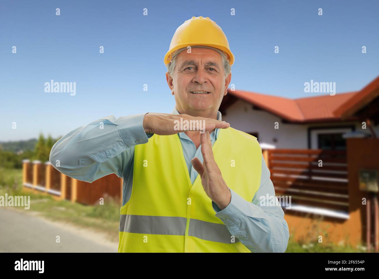 Old male constructor with house background making pause timeout gesture ...