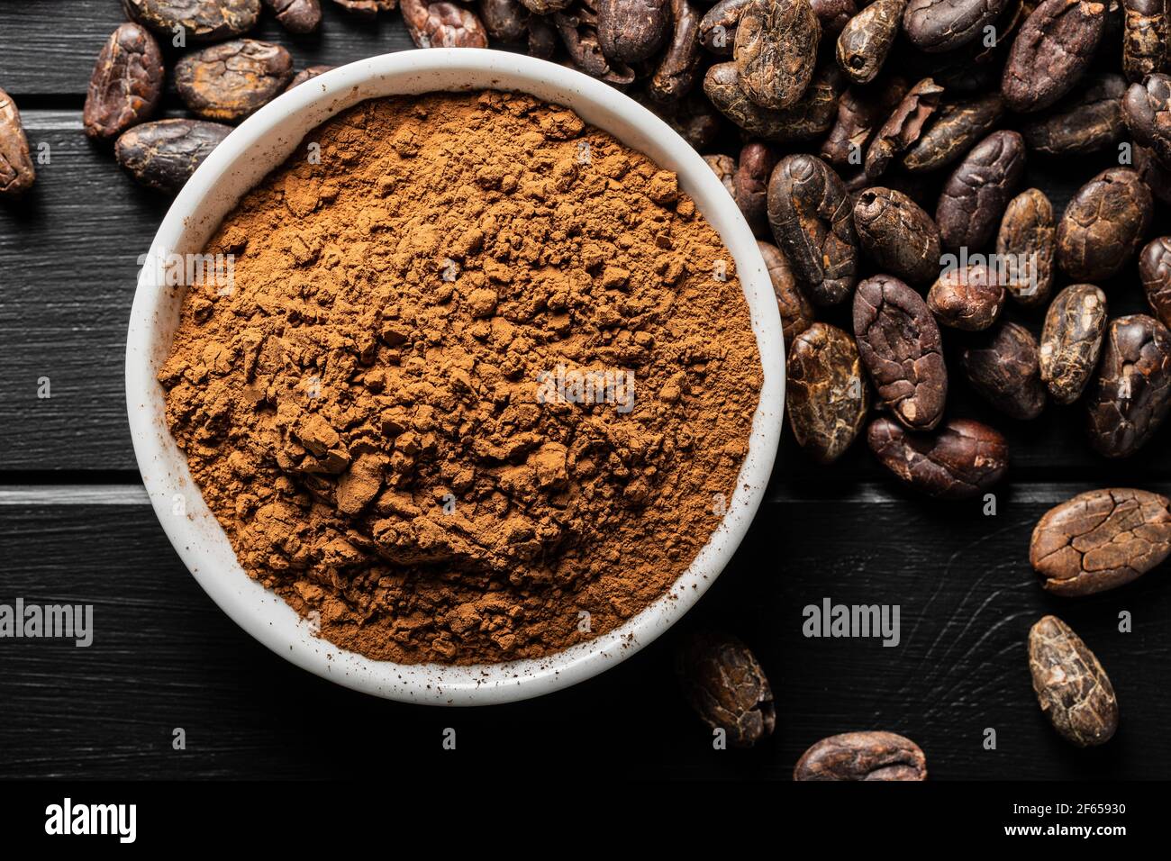 Roasted cocoa beans and cocoa powder in bowl on black table. Top view ...