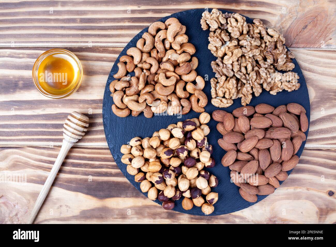 Various nuts sorted in glass bowl with honey bowl and honey dipper ...