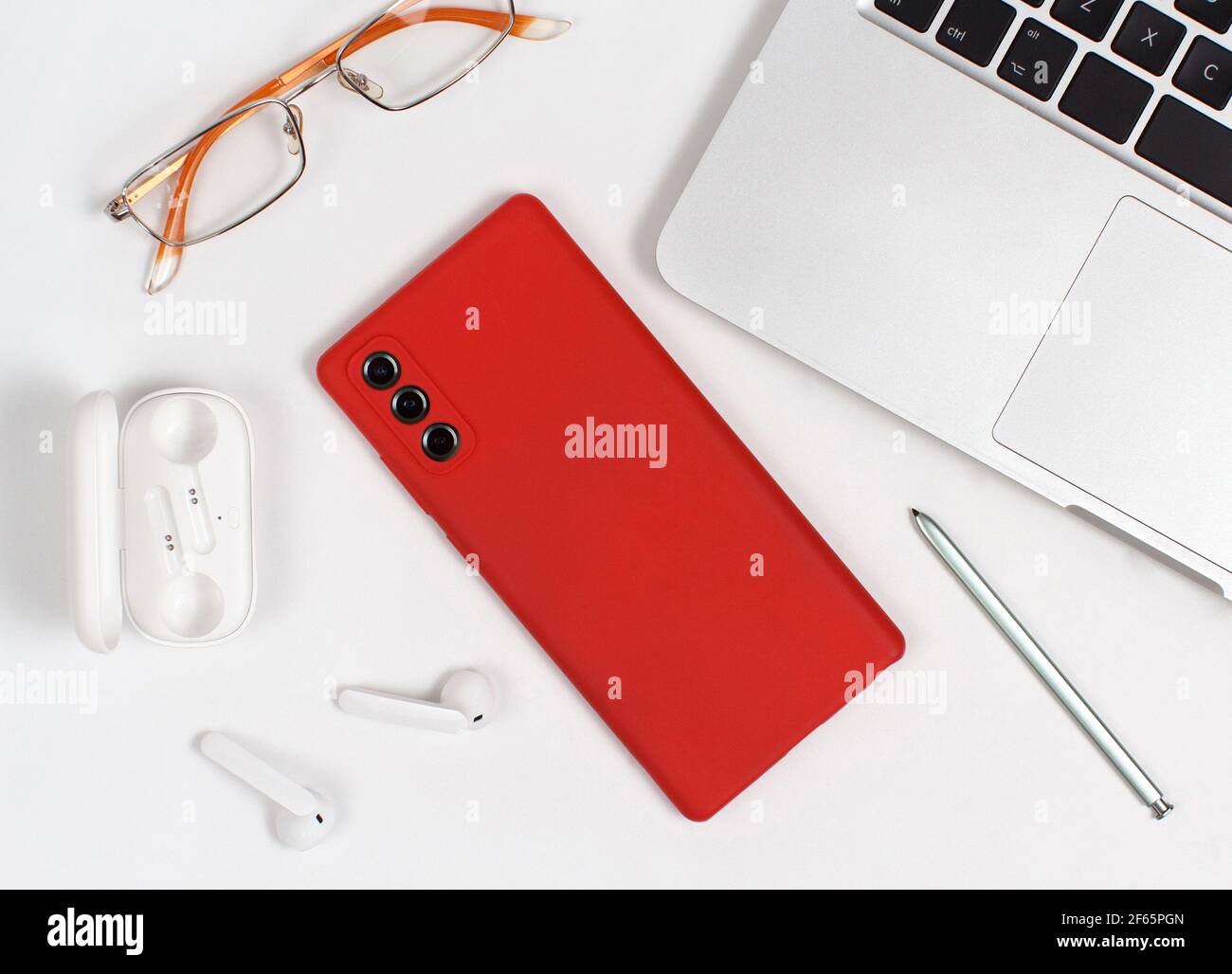 Red Mobile phone, earphones and glasses near laptop on white background ...