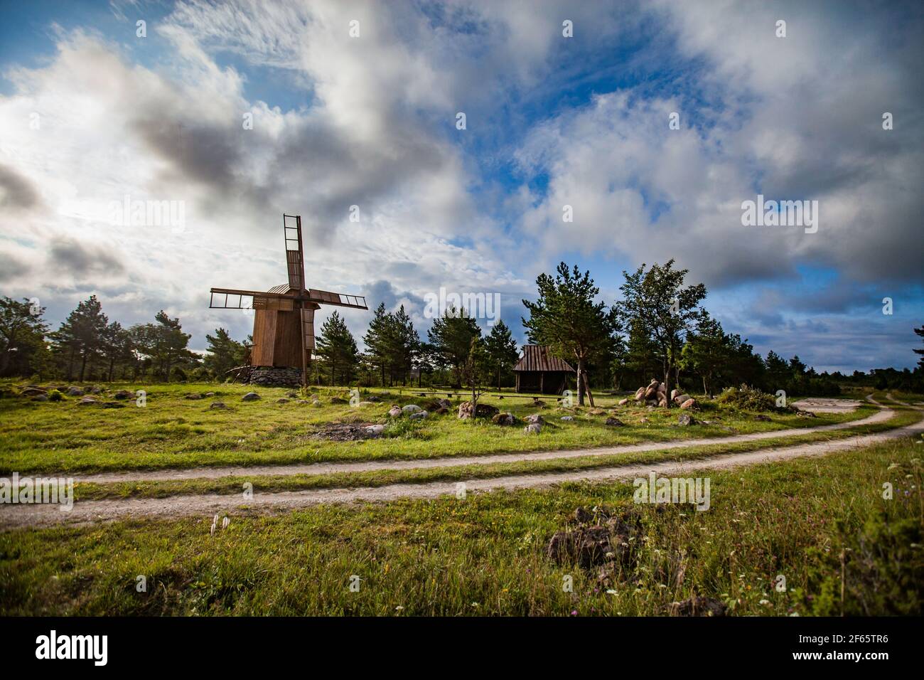 Wooden windmill in field with stones and trees. Rural road. Countryside ...