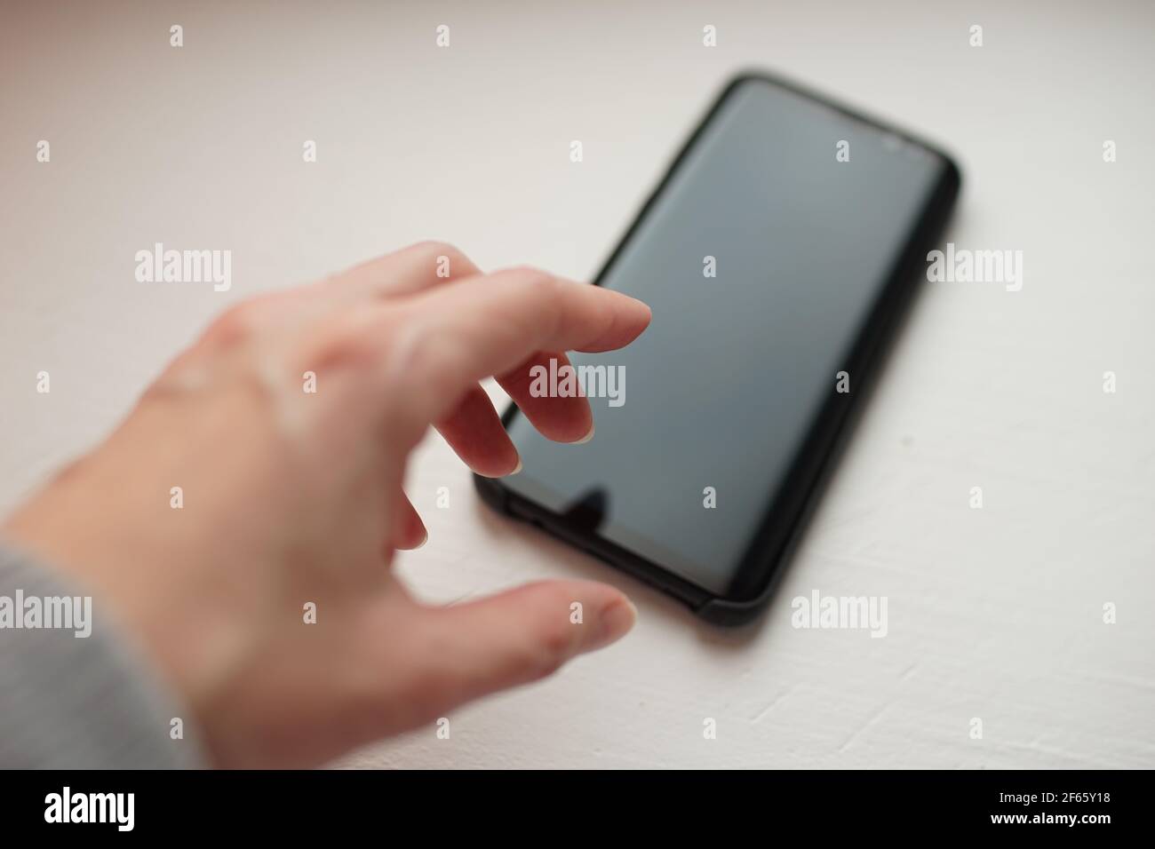 Female hand reaching for black smartphone on white table Stock Photo ...