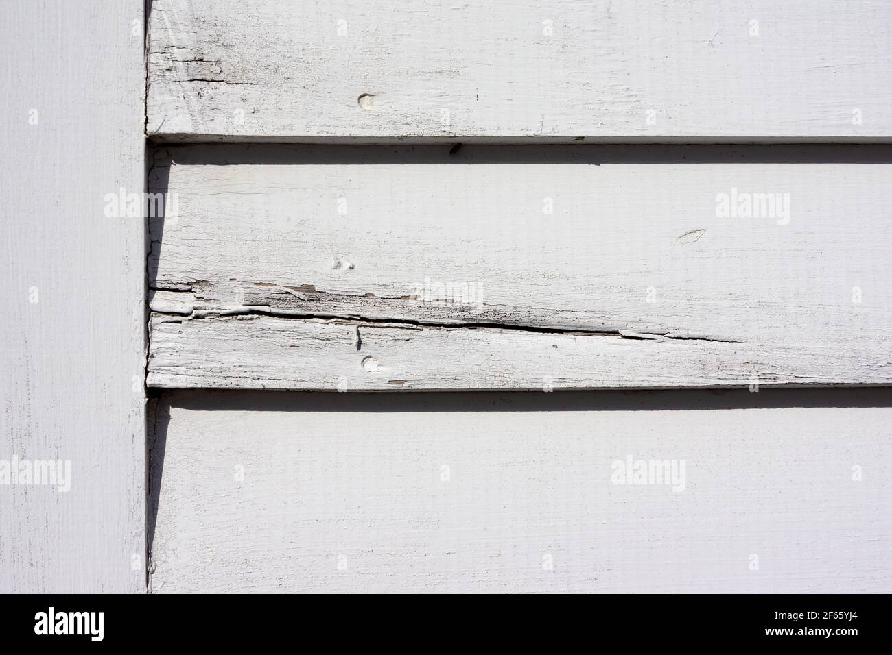 Old clapboard siding painted white next to a trim board showing cracks ...