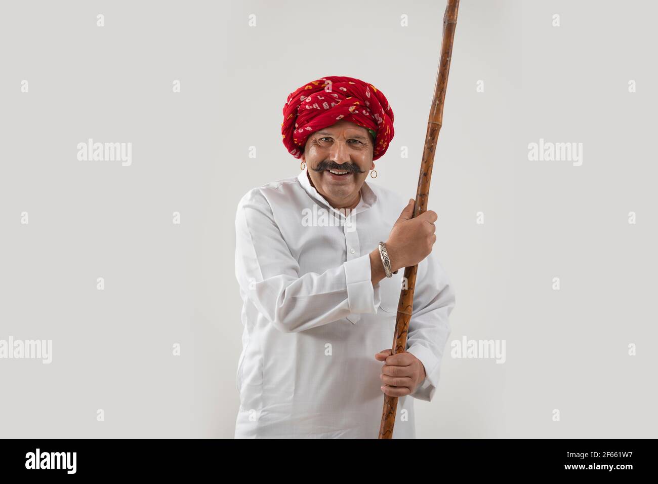 A RURAL MAN HAPPILY STANDS IN FRONT OF CAMERA WITH A LONG STICK IN HAND ...