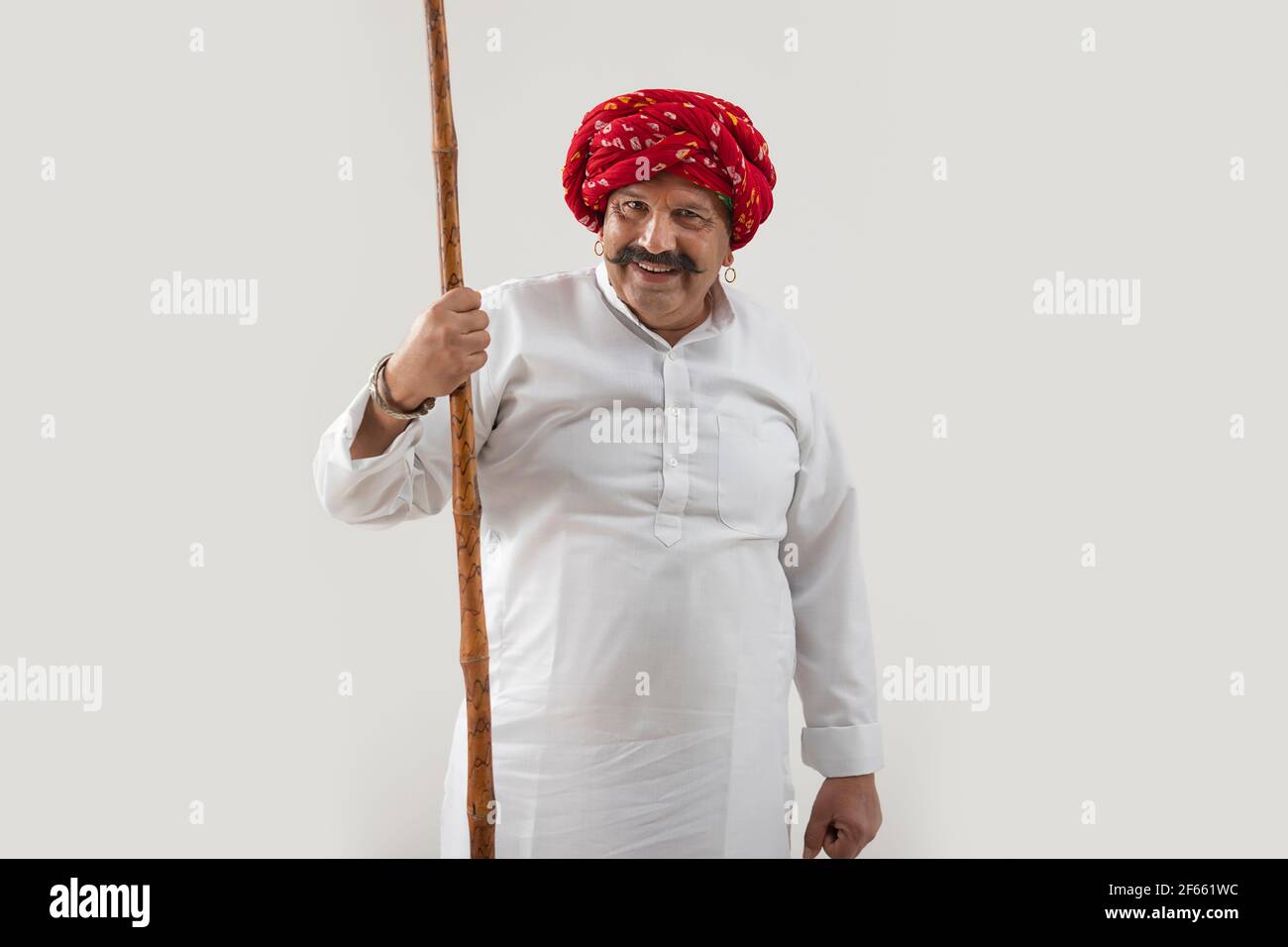 A VILLAGER HAPPILY STANDS IN FRONT OF CAMERA WITH A LONG STICK IN HAND ...