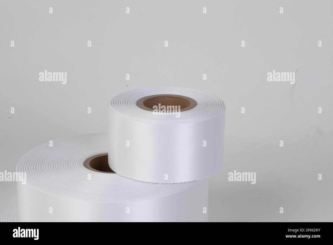 macro side view tower of two coils of white satin ribbons of different ...