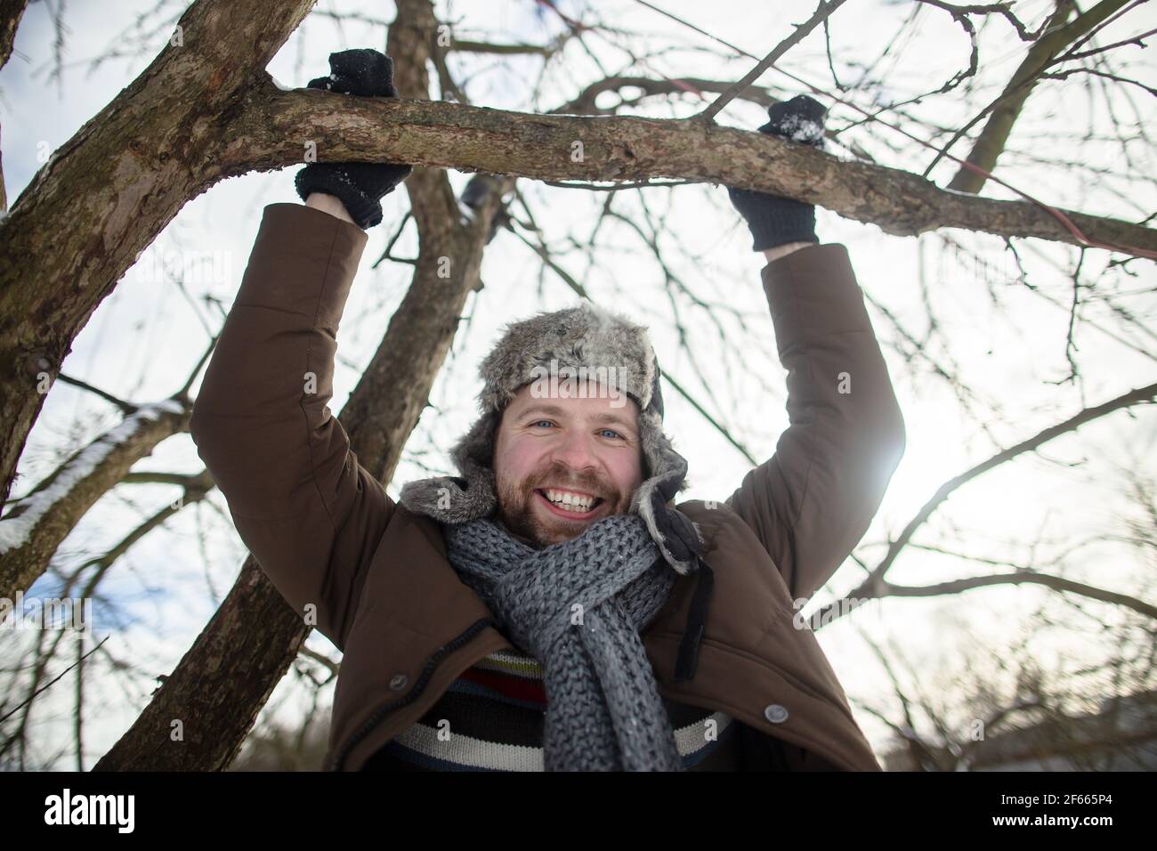 Funny, happy man holds hands to a tree branch, looks at the camera and ...