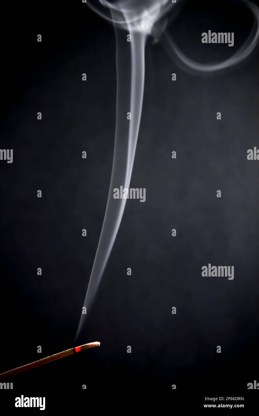 Incense stick lit and fuming on black background Stock Photo - Alamy