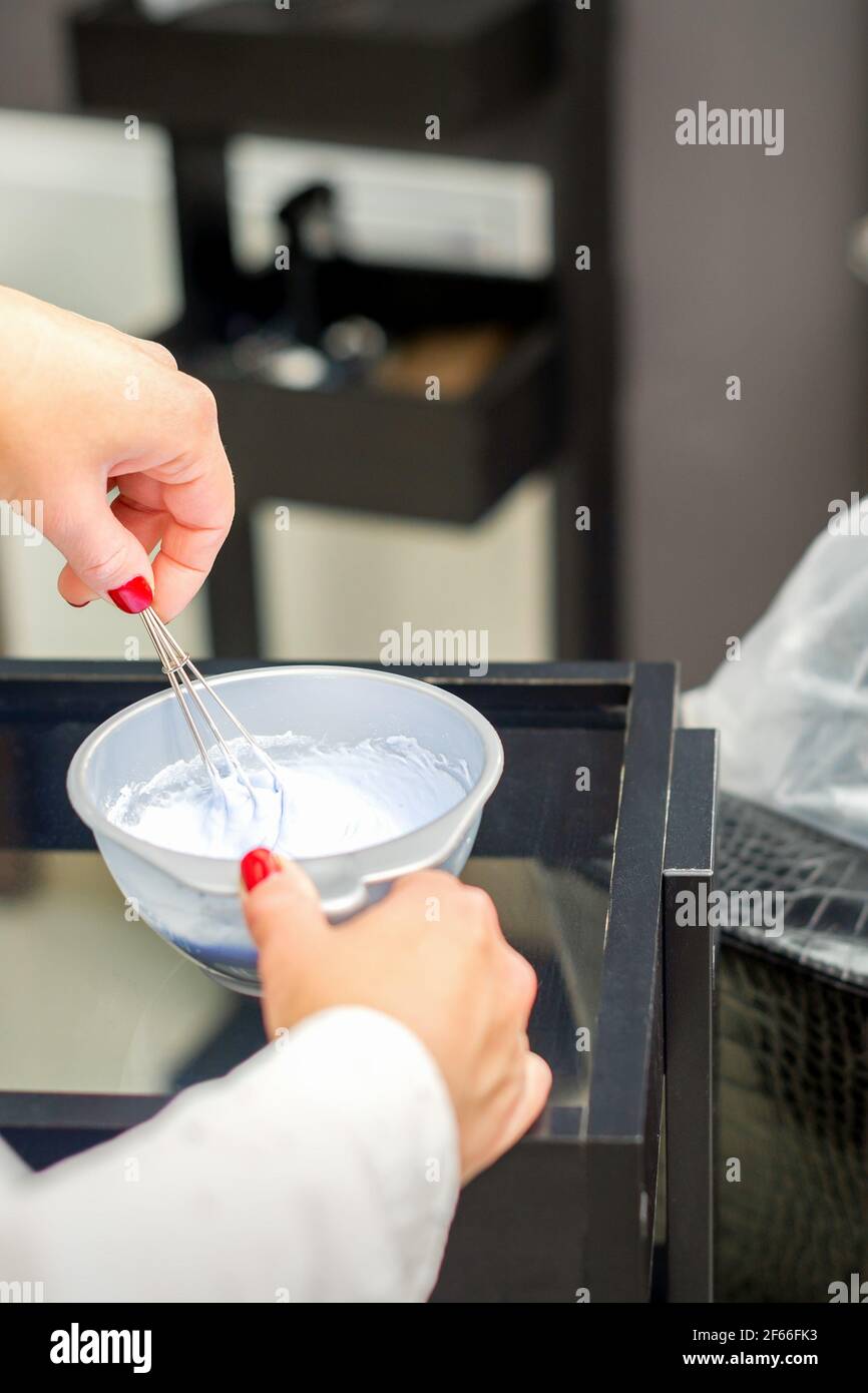 The hairstylist makes a white color dye mix for coloring hair at a ...