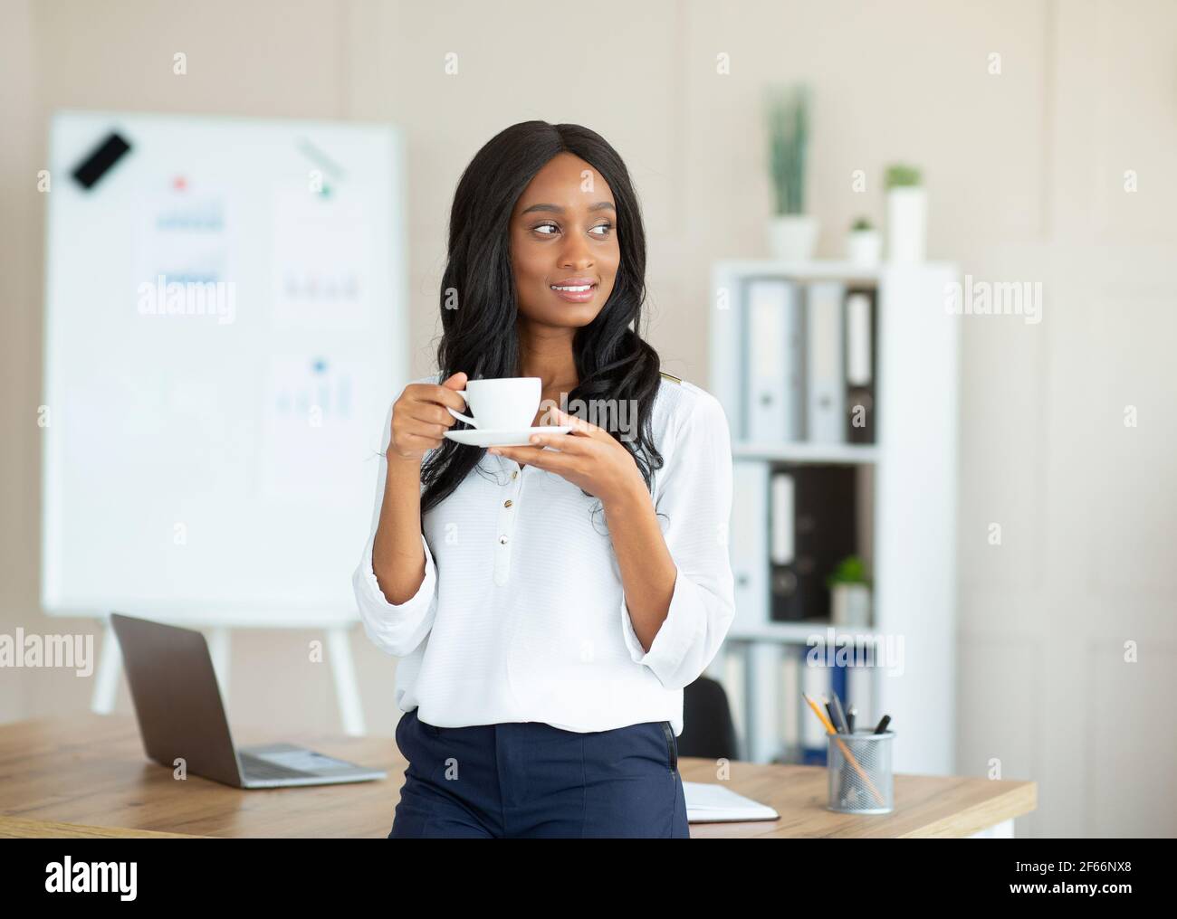 Portrait of charming black female manager in formal wear drinking ...