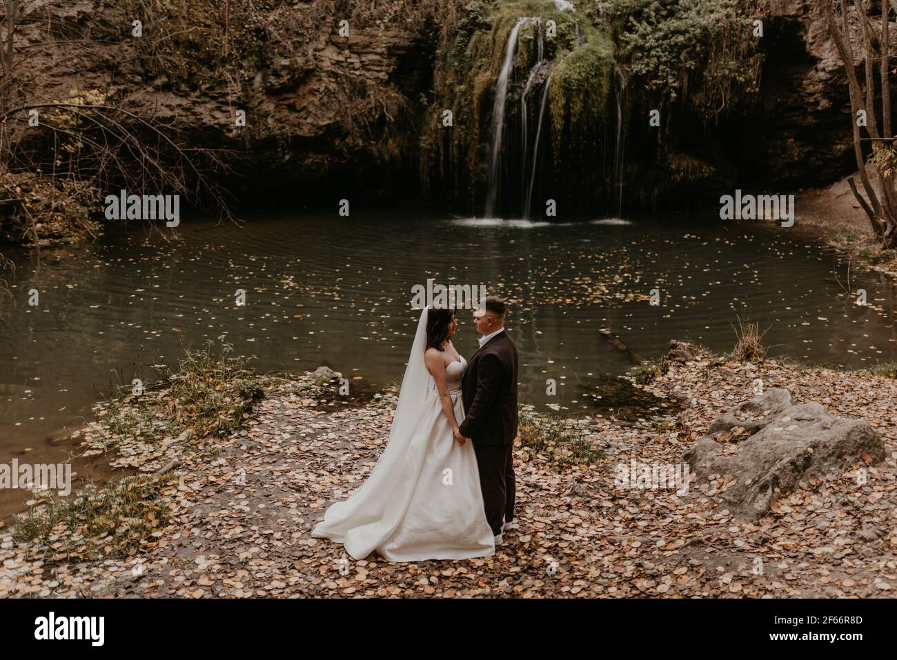 skinny bride in white wedding dress and long veil hugs groom in a suit ...