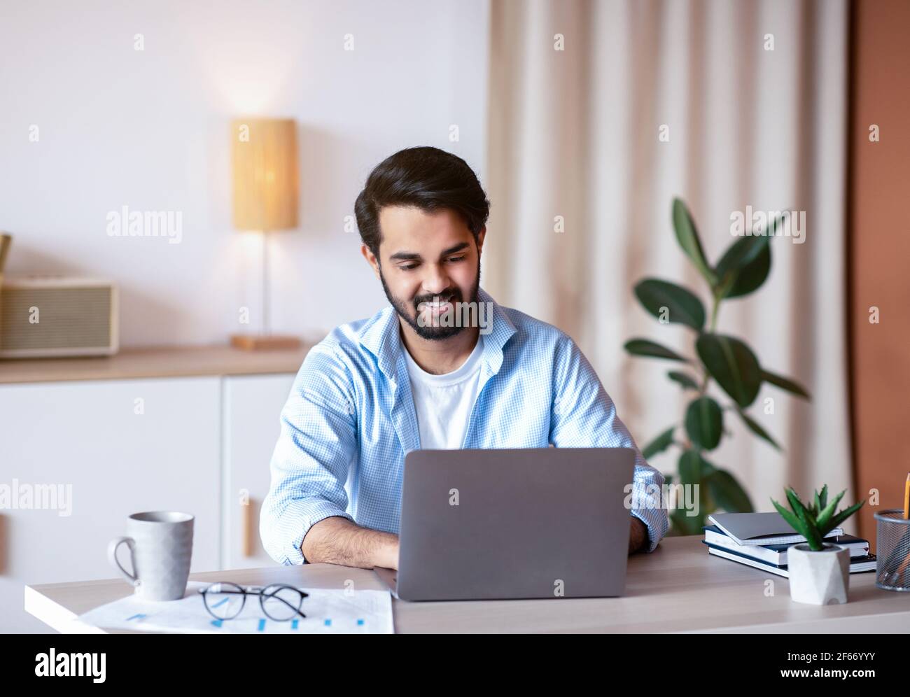 Cheerful Eastern Man Sitting At Desk In Home Office, Working On Laptop ...
