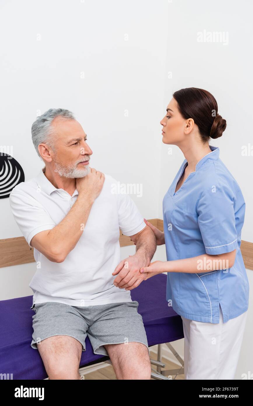mature man touching shoulder during consultation with rehabilitologist ...
