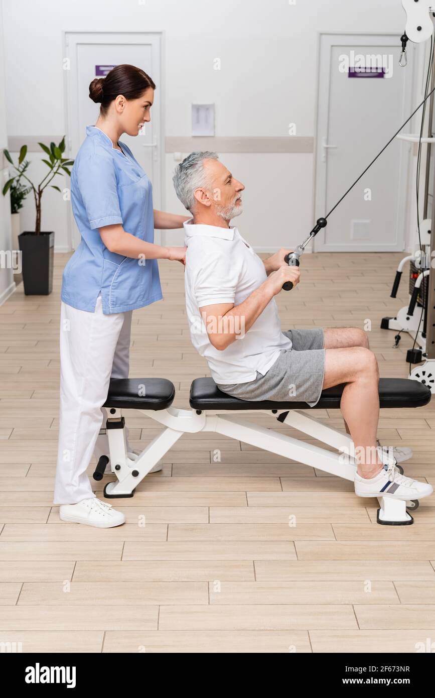 side view of physical instructor supporting mature man during ...