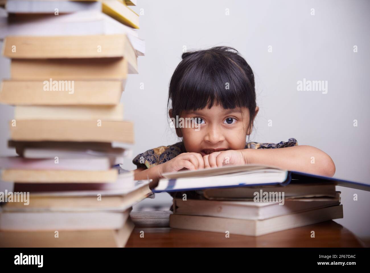 Cute little girl with pile of books to study and doing homework at home ...