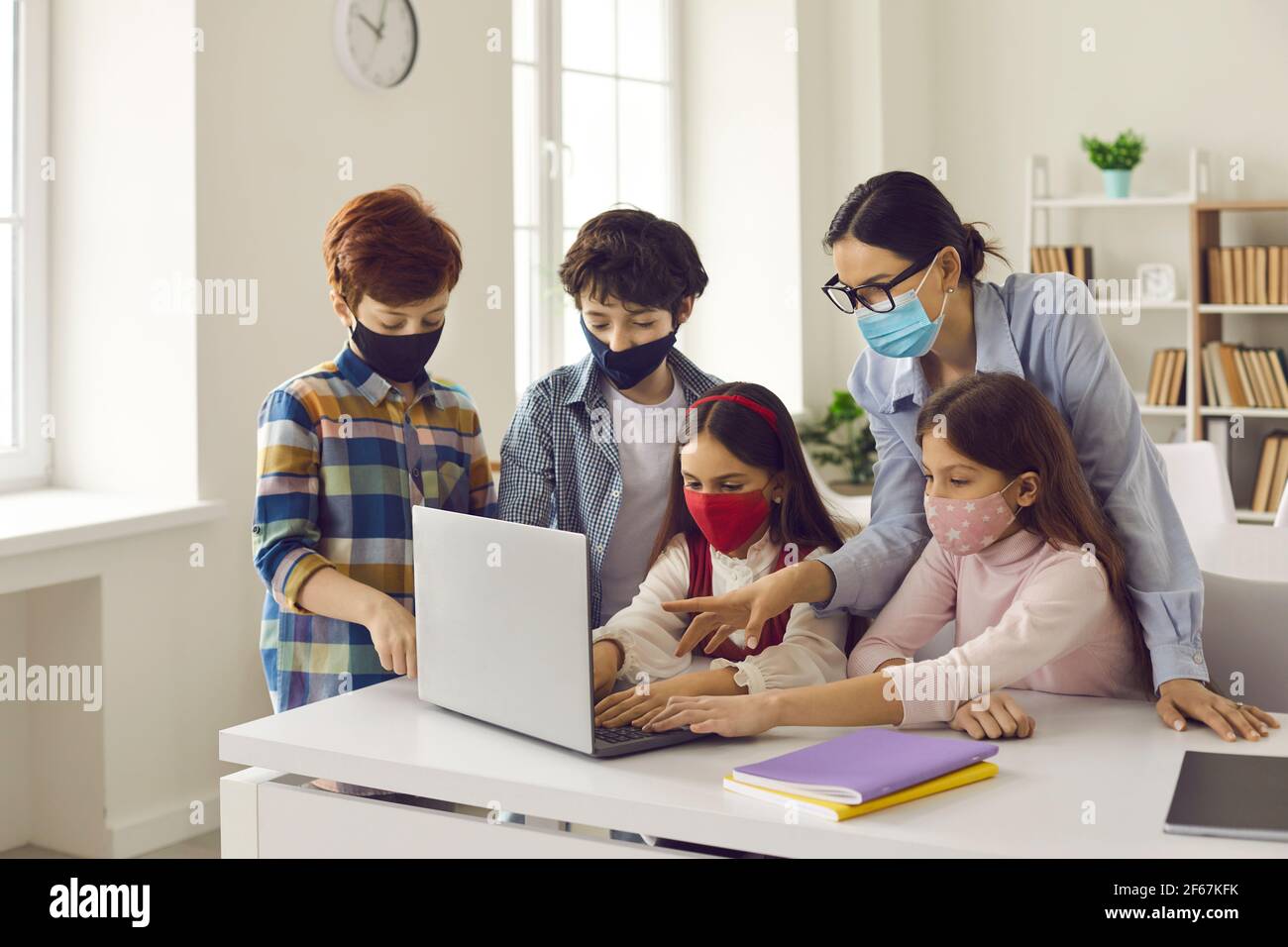 School students and teacher in medical face masks coding game on laptop ...