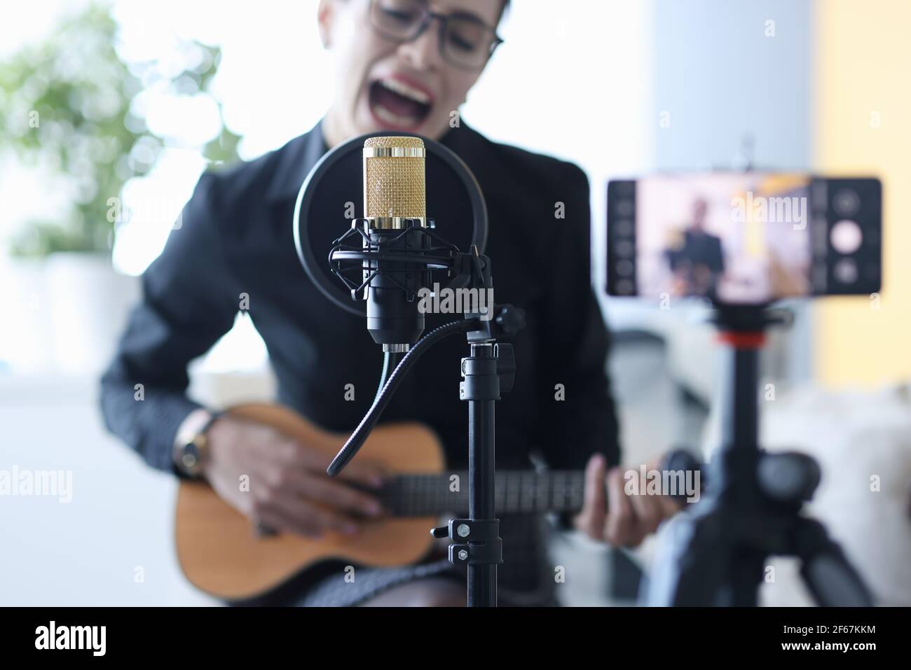 Woman singing song and playing ukulele and filming with mobile phone ...