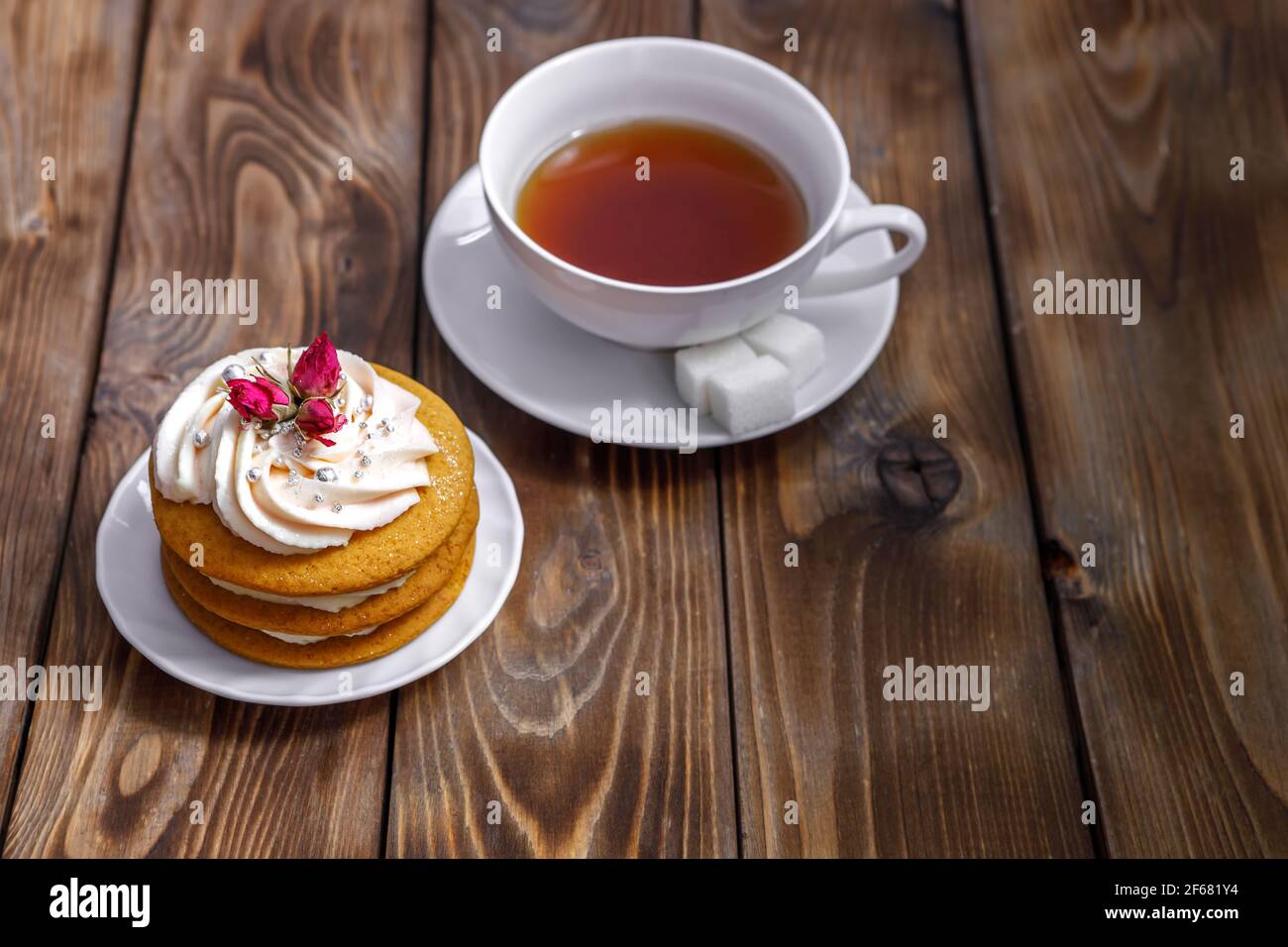 Sponge cake with cream, decorated with small flowers and a cup of tea ...