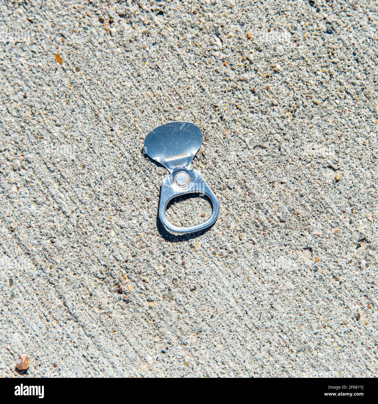 A discarded metal can tab lays on a concrete curb Stock Photo - Alamy