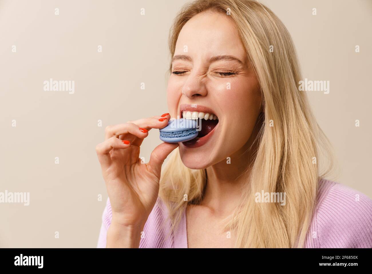 Cheerful beautiful girl eating macaroon with eyes closed isolated over ...