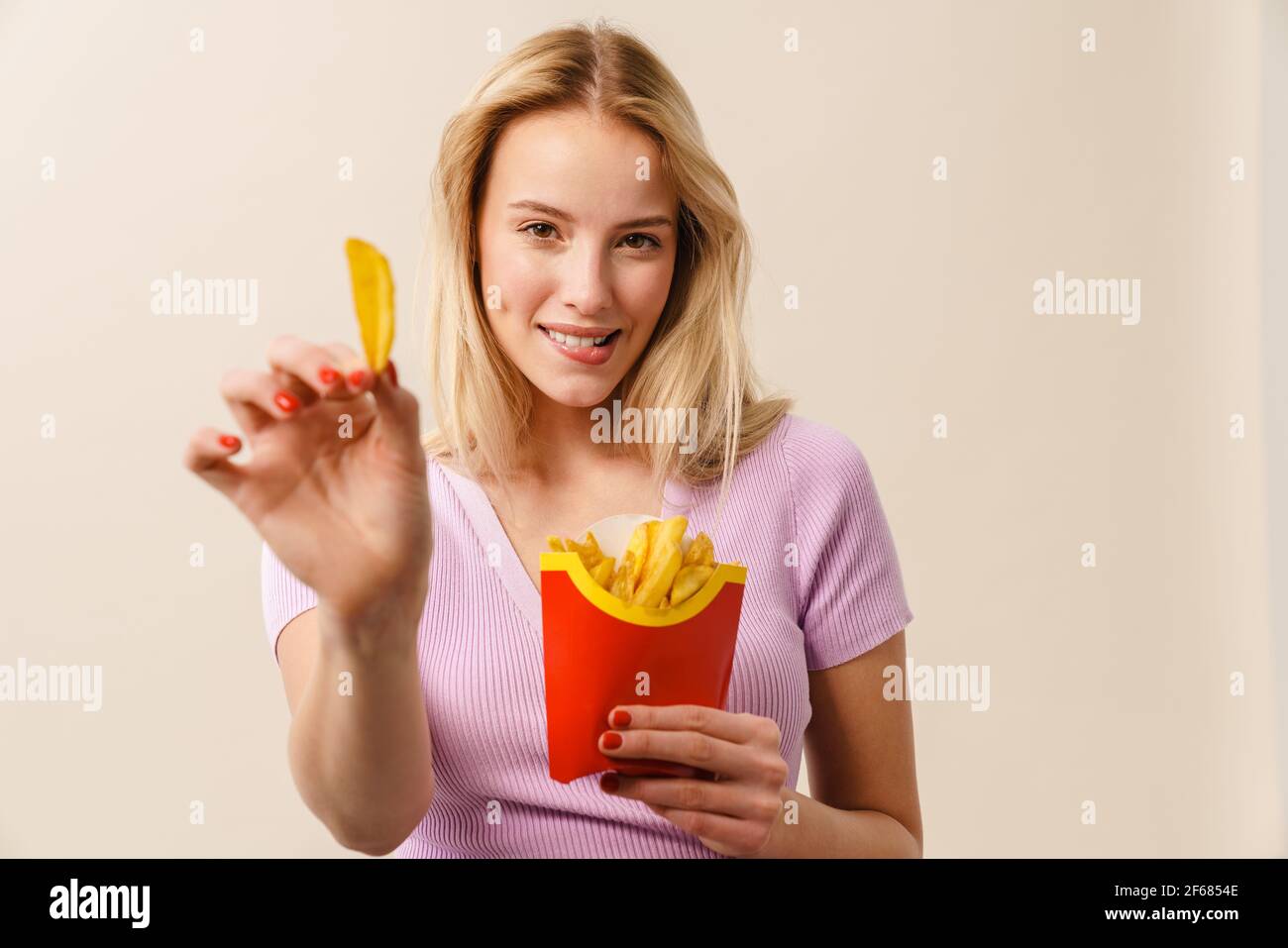 Cheerful beautiful girl smiling while showing french fries at camera ...