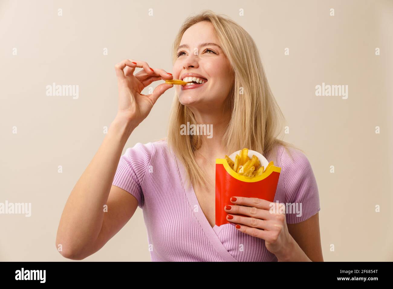 Cheerful beautiful girl laughing while eating french fries isolated ...