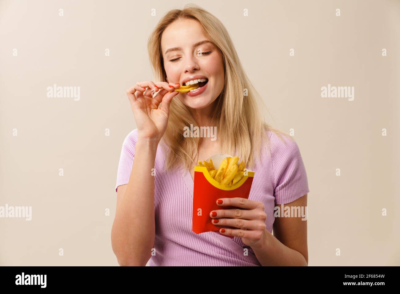 Cheerful beautiful girl laughing while eating french fries isolated ...